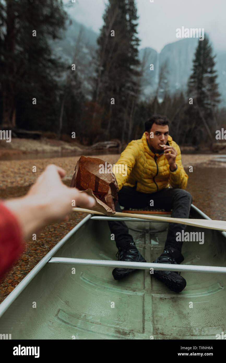 Young canoeing couple sharing snacks on canoe, personal perspective ...
