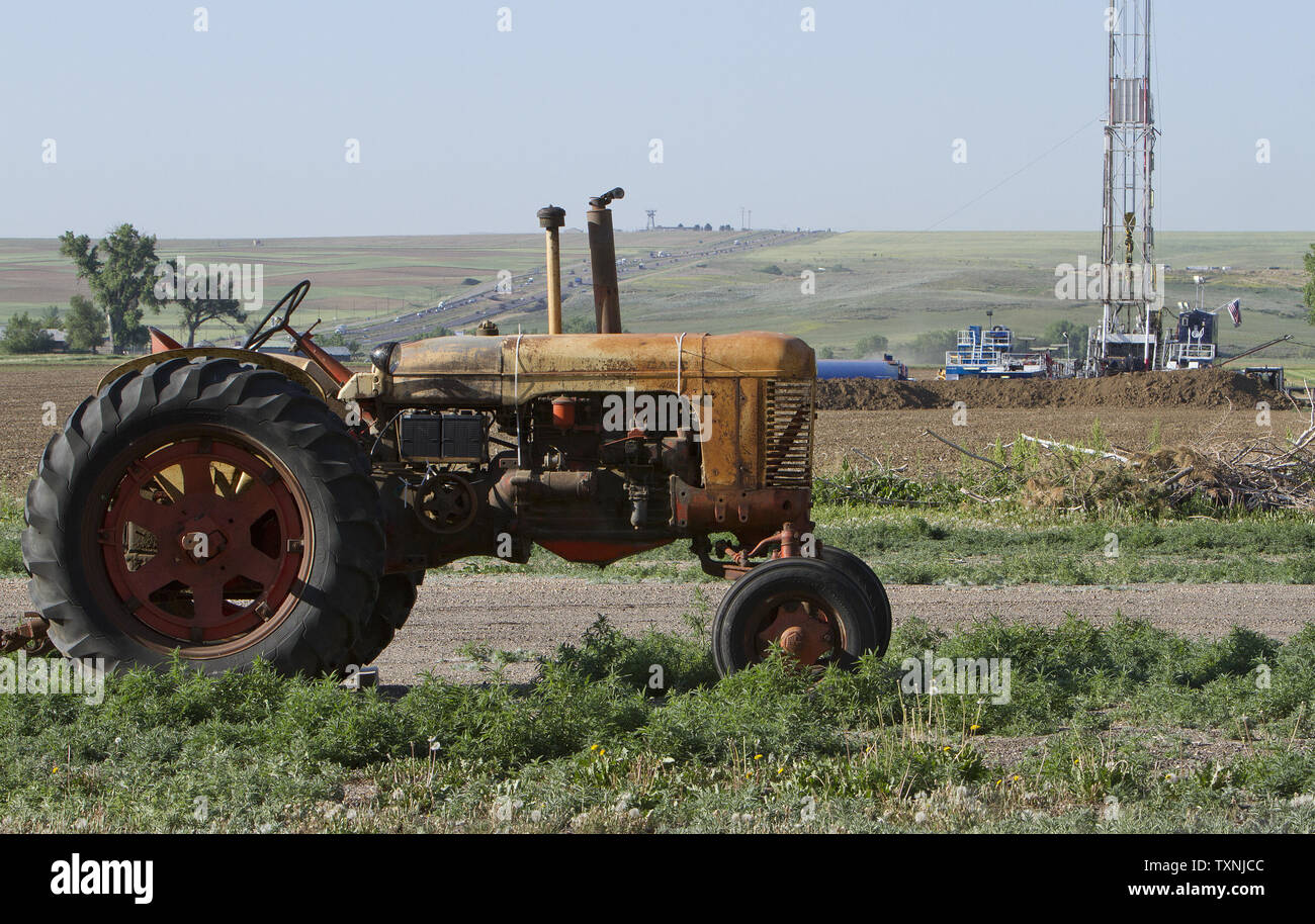 An aging tractor shares land with a oil drilling rig at a farm above ...