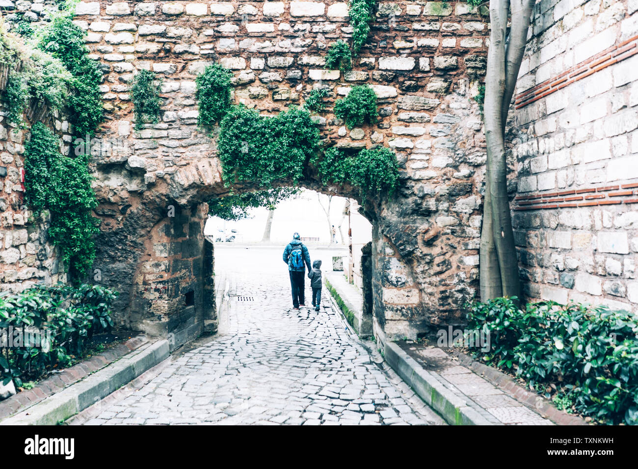 An adult man and child pass through a paved street through a narrow ...