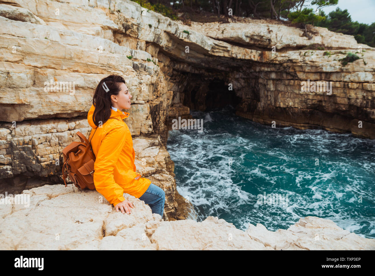 young woman sitting at cliff looking at grotto cave with blue azure ...