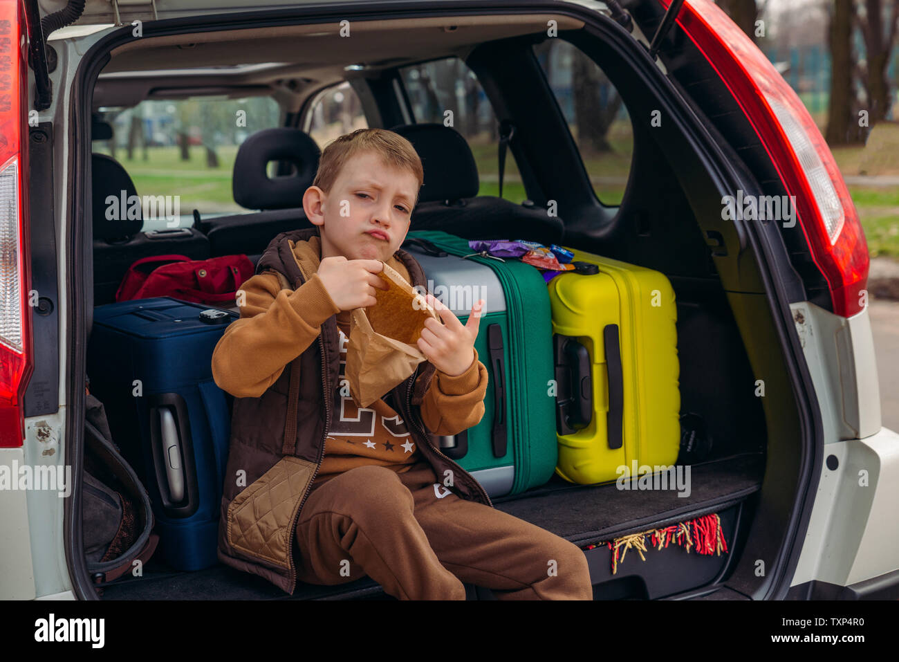 little kid looking into paper bag with candies sitting in car trunk ...