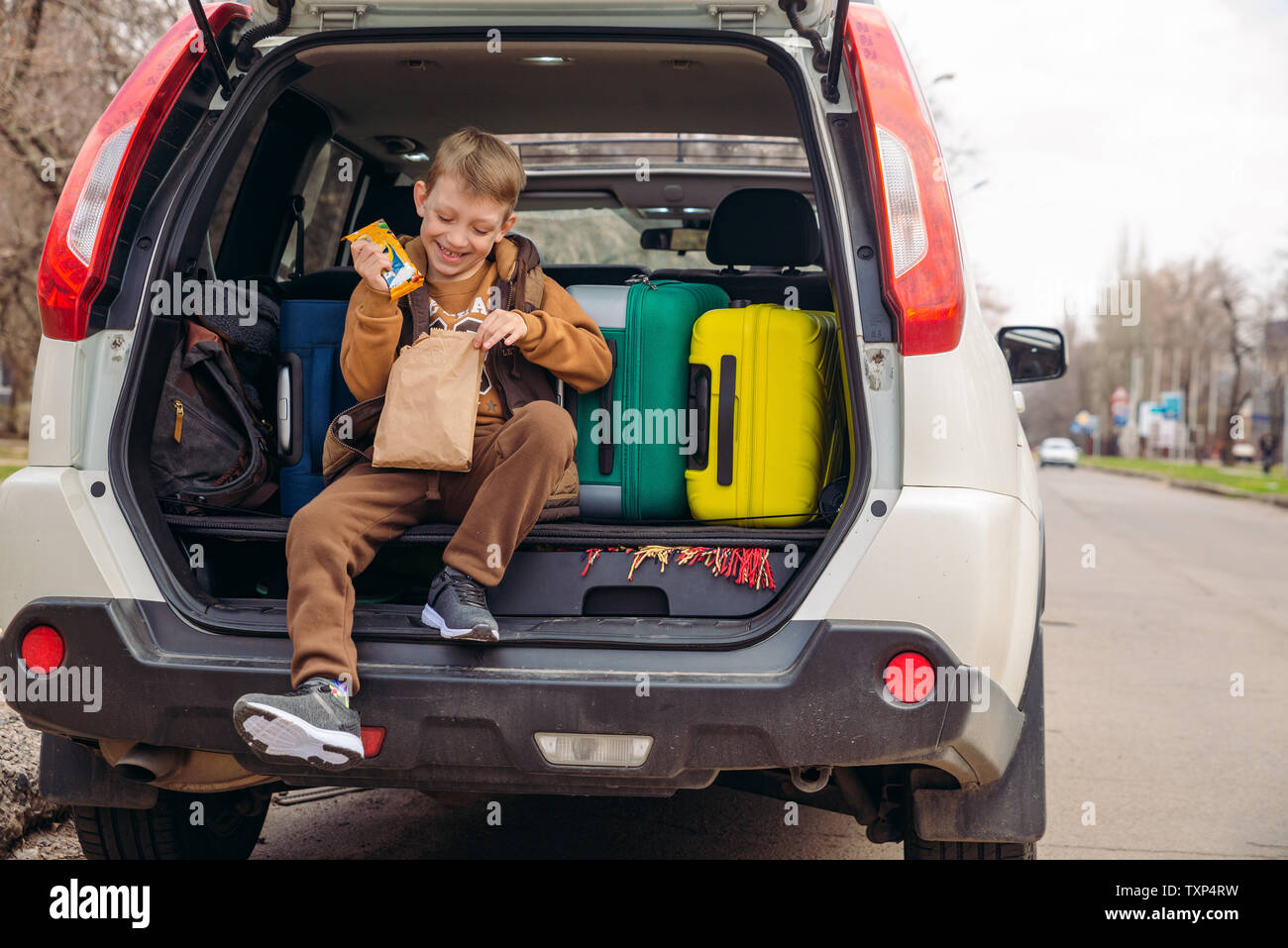 little kid looking into paper bag with candies sitting in car trunk ...