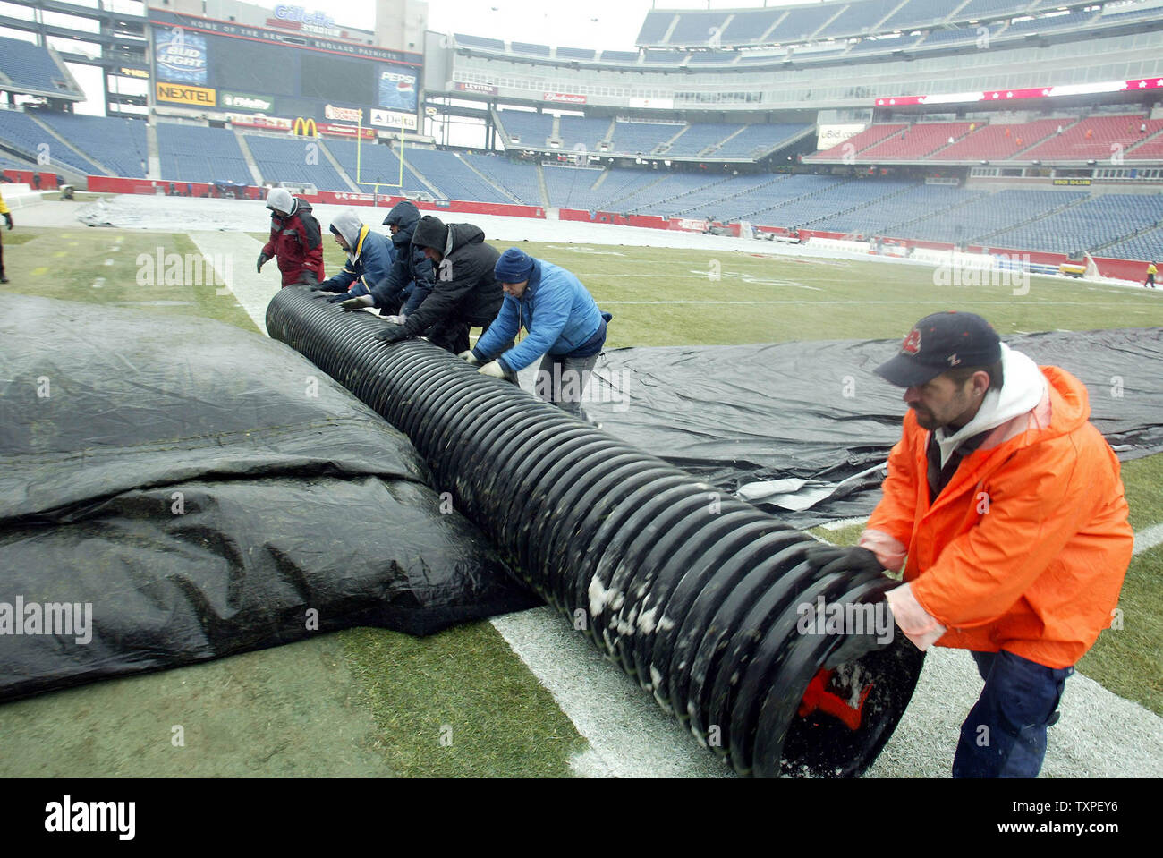 Ground crew members at Gillette Stadium remove a tarp from the field ...