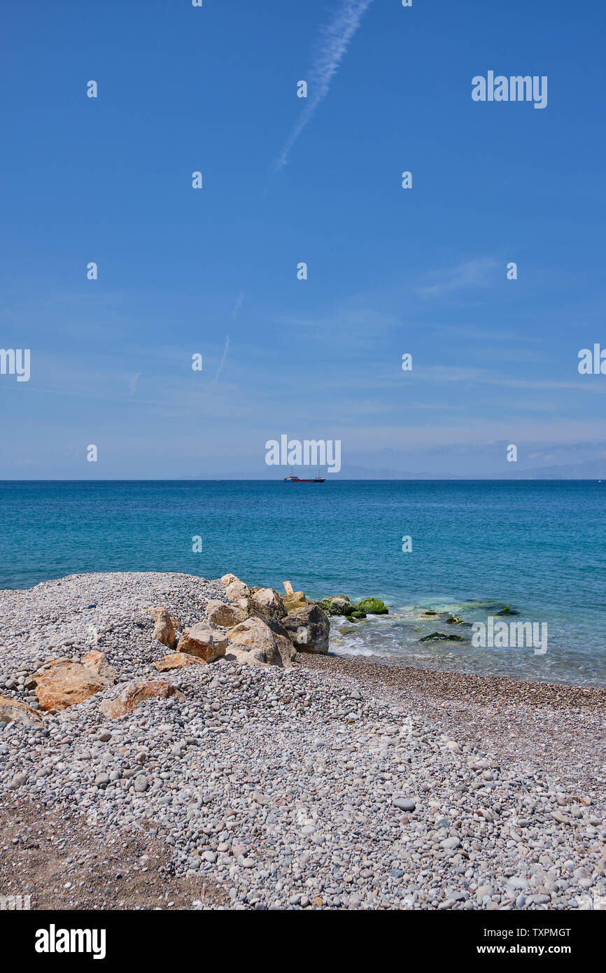 pebble beach in the foreground and a ship on the sea in the background ...