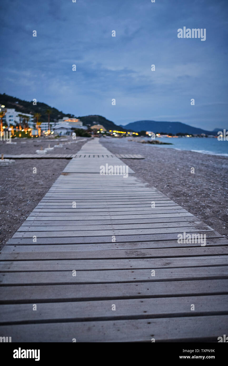 wooden footpath on a rocky beach sea on the right side and hotel on the ...