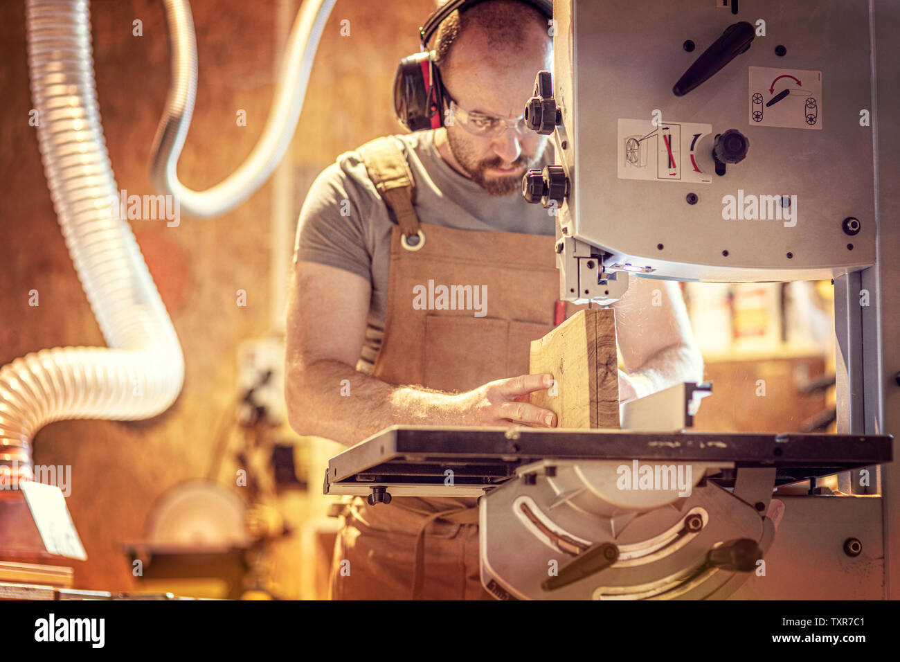 portrait of a carpenter inside his carpentry workshop using a band saw ...