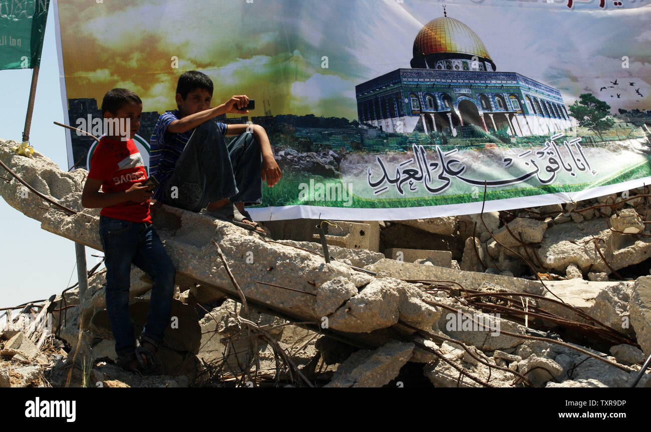 Palestinian children sit atop a destroyed house beside a picture of the ...