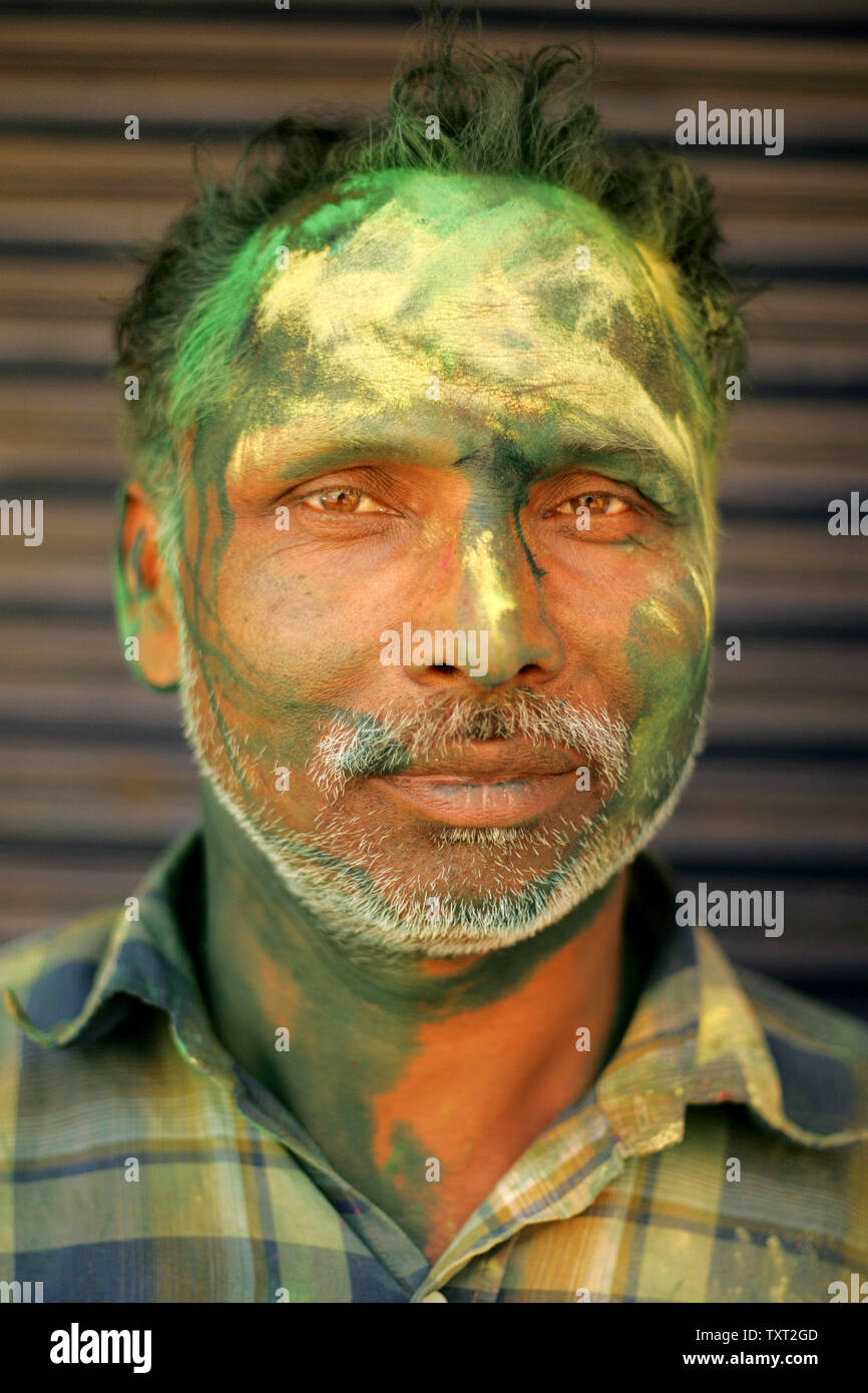 An Indian man with a face smeared with colored powder poses for a ...