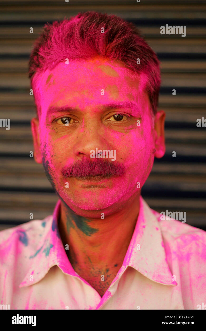 An Indian man with a face smeared with colored powder poses for a ...