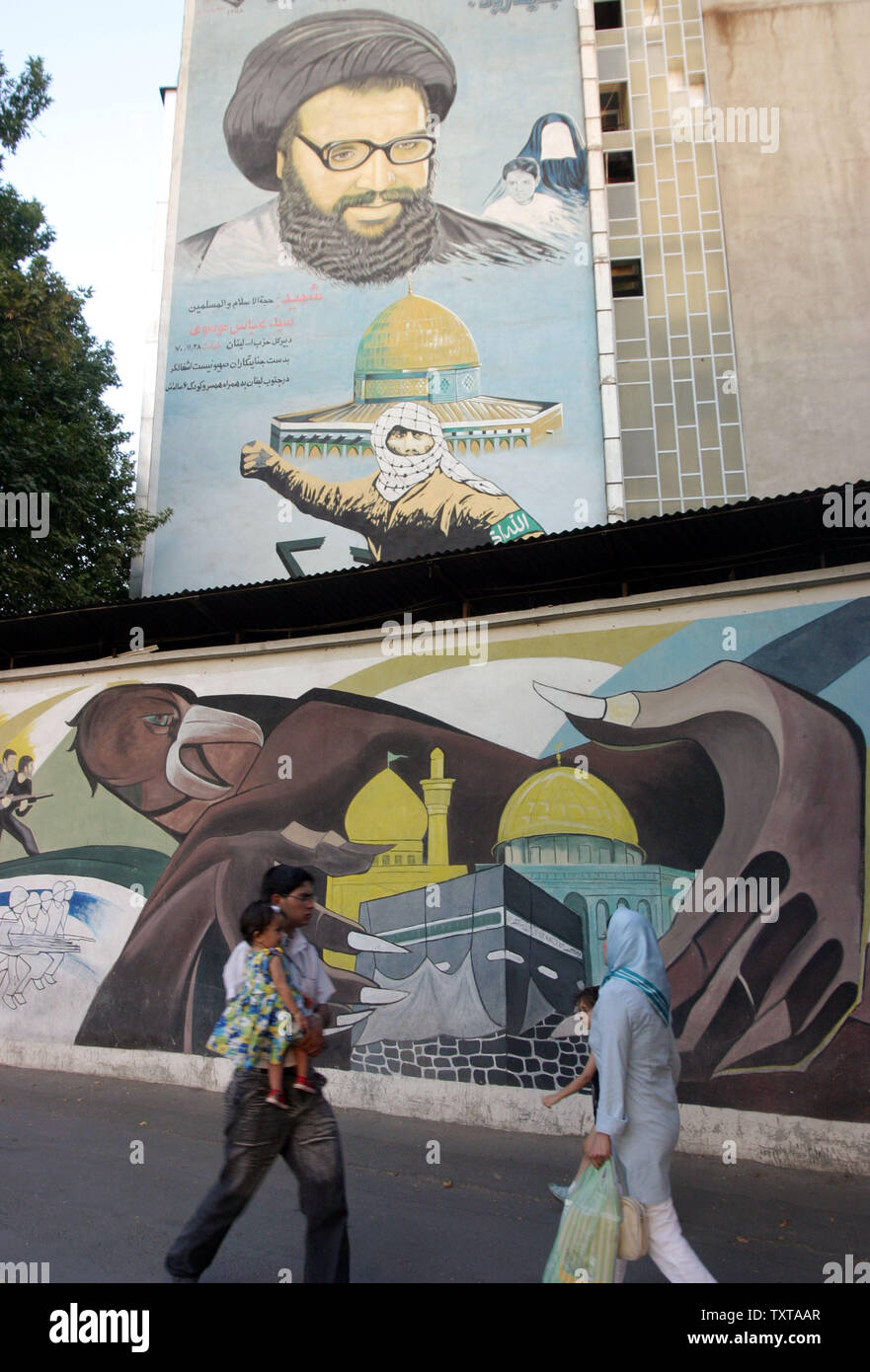 Iranian people walk past a mural covered wall that is full of paintings ...