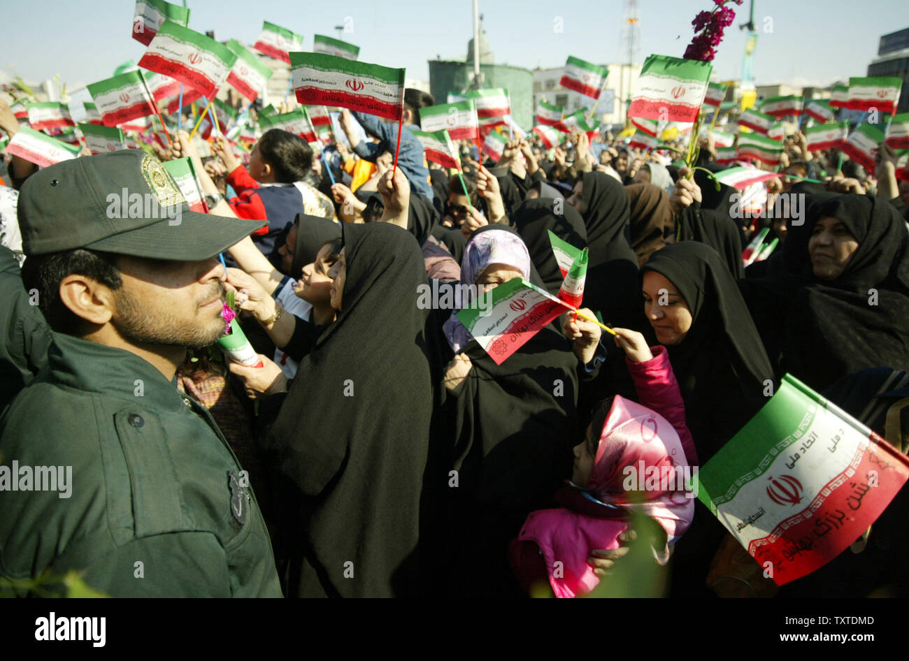 An Iranian police officer stands guard as another wave their national ...