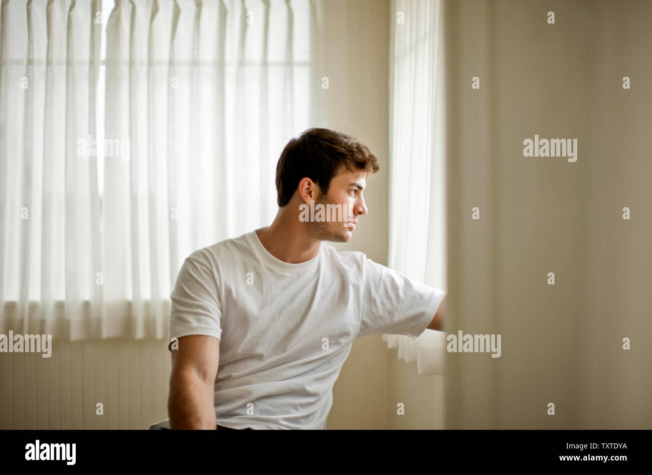 Young man looking out the window of his house Stock Photo - Alamy