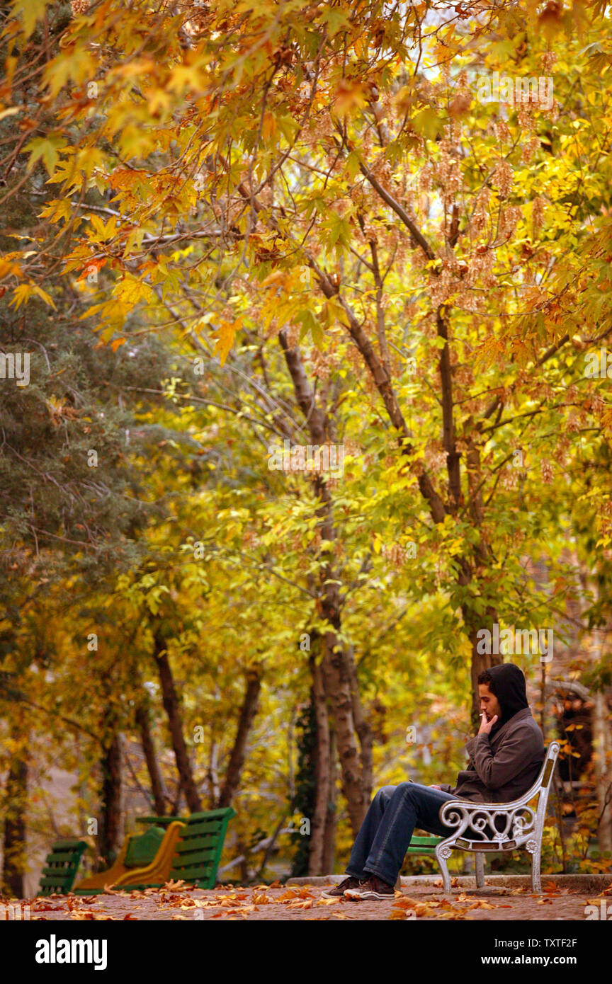 An Iranian man smokes cigarette under trees during fall in Niavaran ...