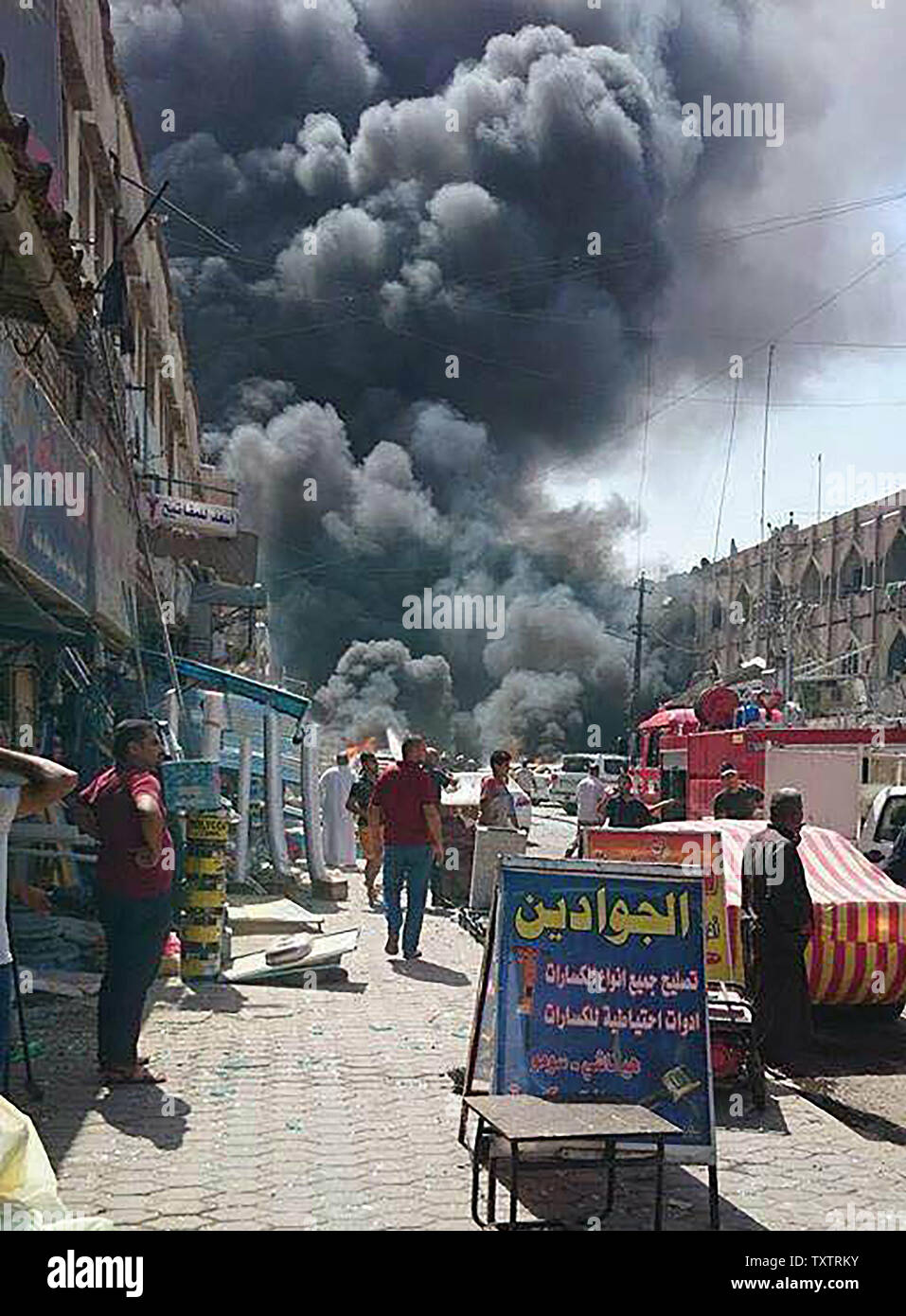 Iraqi firefighters extinguish a fire as civilians gather after a car ...