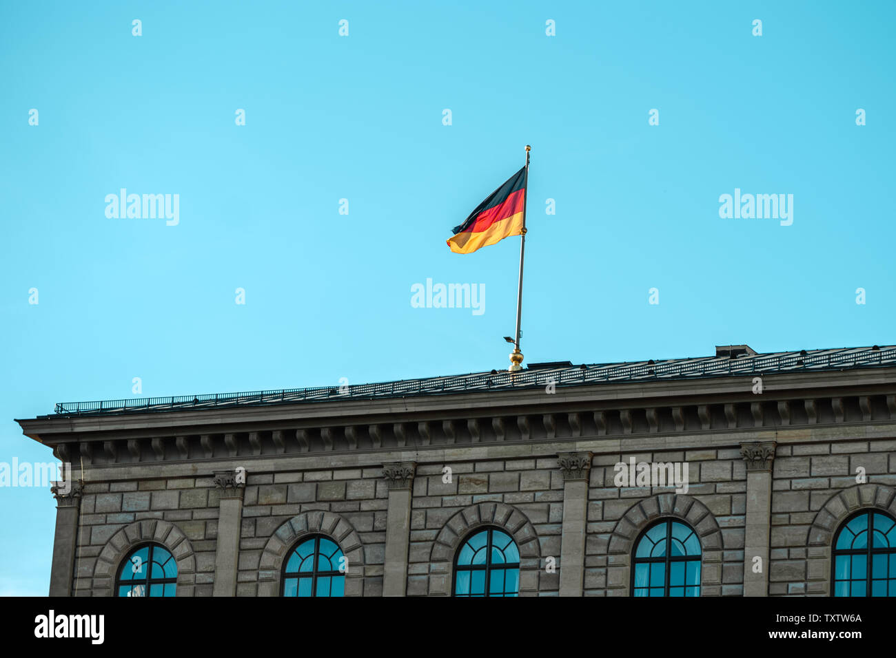 German flag waving on silver flagpole, building in Munich. Blue sky ...