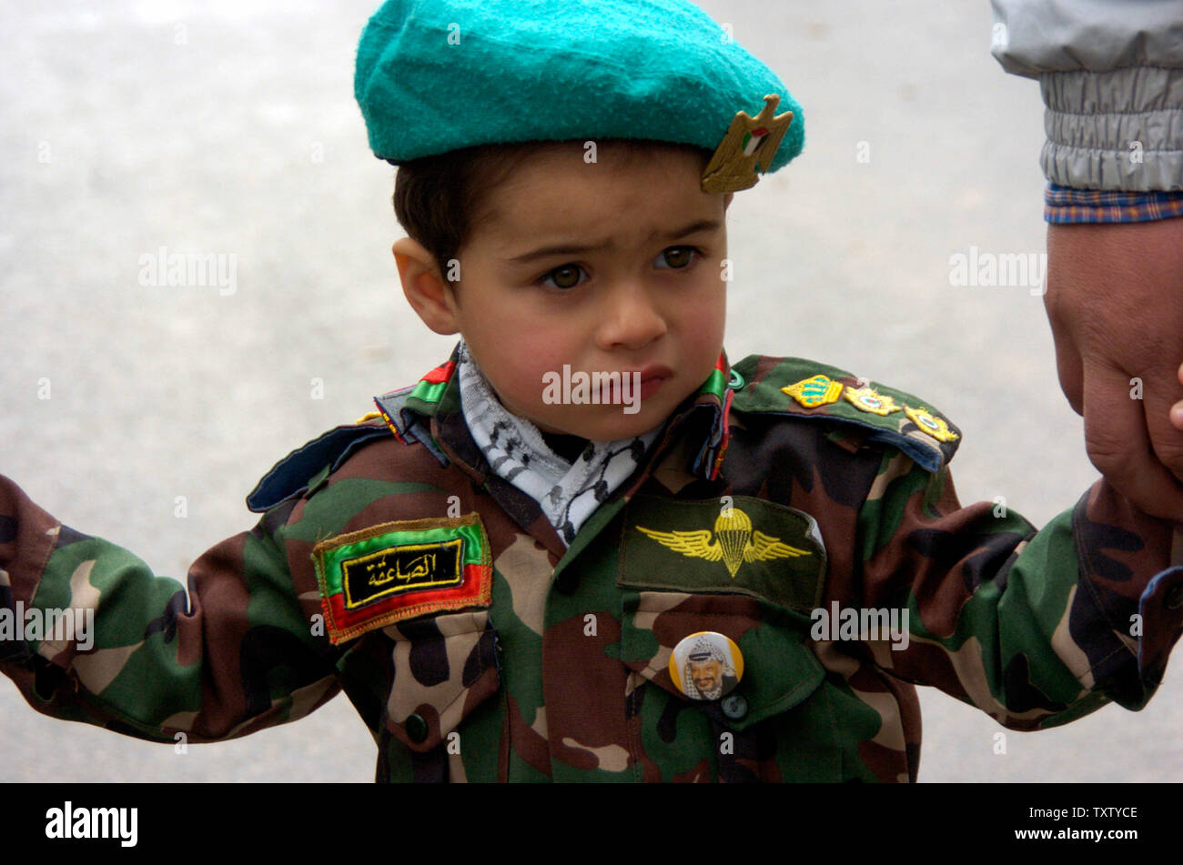 A Palestinian boy wears an army uniform with a badge with the face of ...