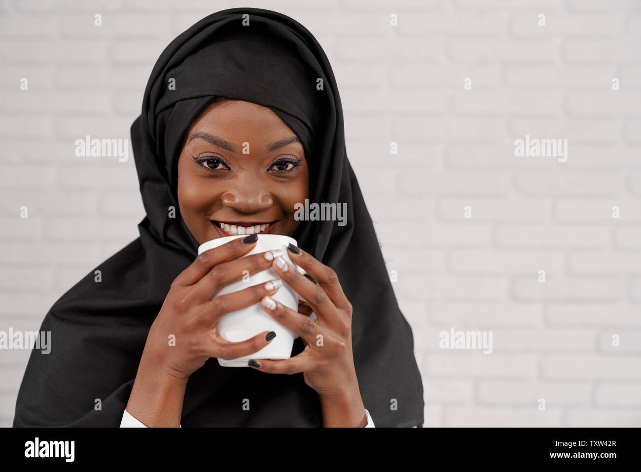 Beautiful, charming muslim woman holding white cup, with perfect smile ...