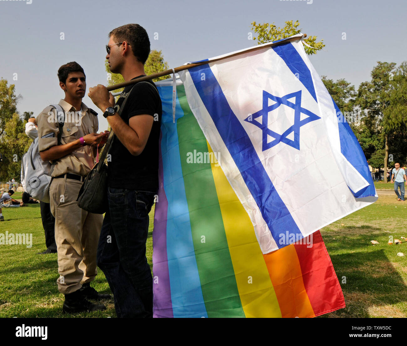 An Israeli soldier talks to a friend holding a rainbow flag and an ...