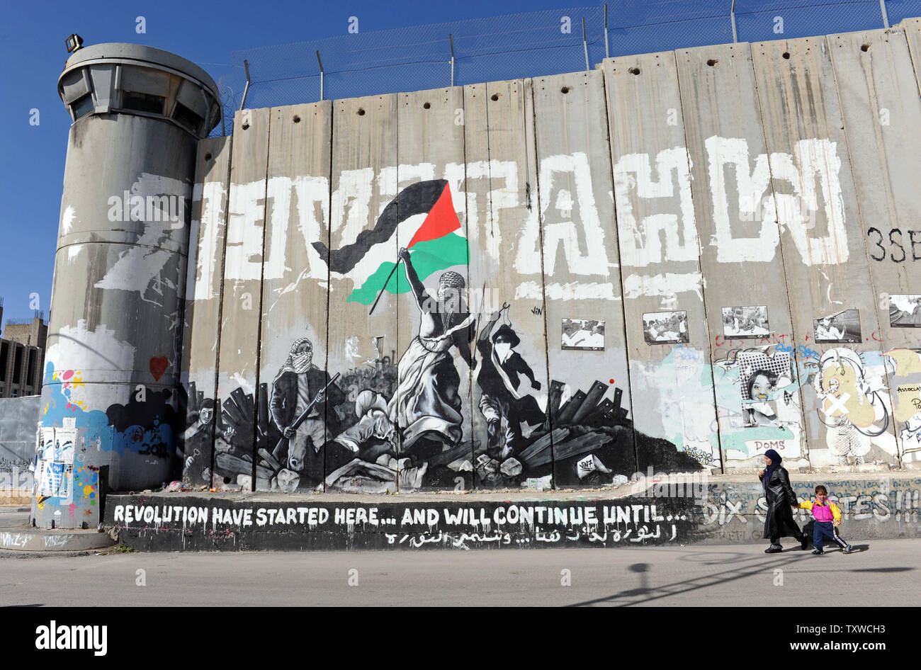 A Palestinian woman and her child walk past a large painting declaring ...