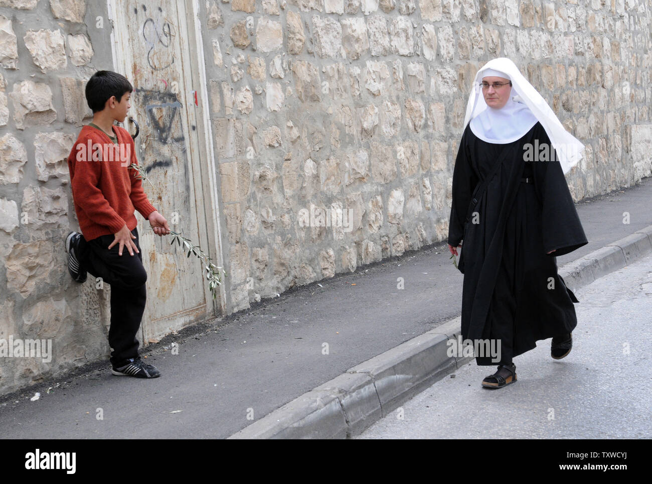 A Catholic nun walks by a Palestinian boy selling olive branches before ...