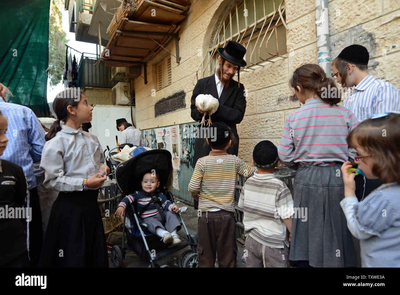 An Ultra-Orthodox Jewish man swings a chicken over his children's heads ...