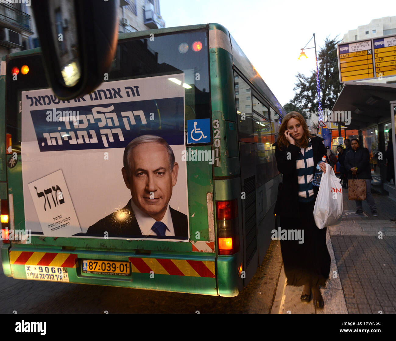 A woman walks past an Israeli bus with an election campaign poster of ...