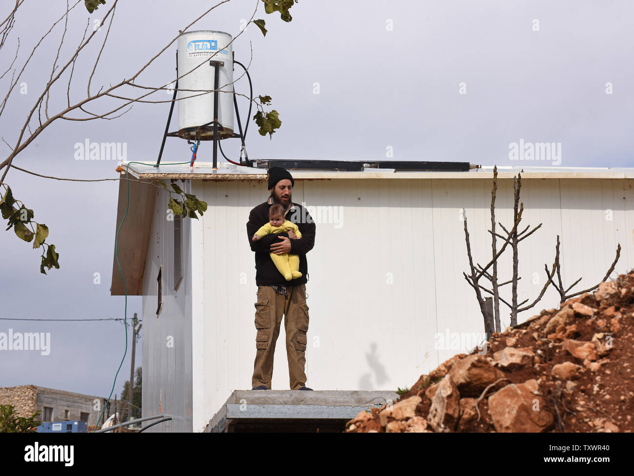 An Israeli settler holds a baby outside his house in the illegal ...