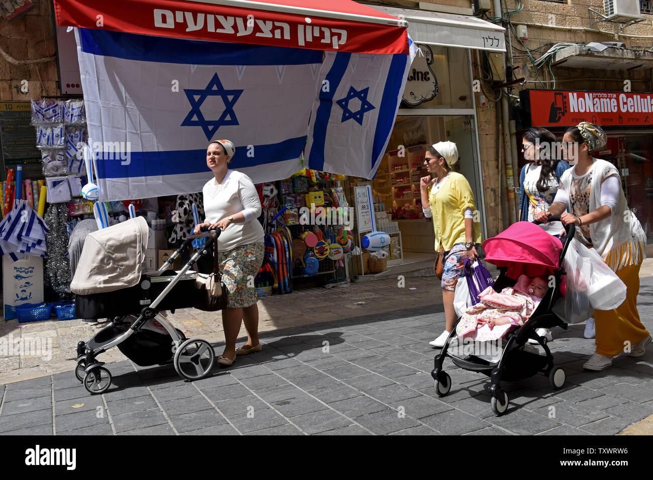 Religous Jewish woman push baby carriages past a store selling Israeli ...