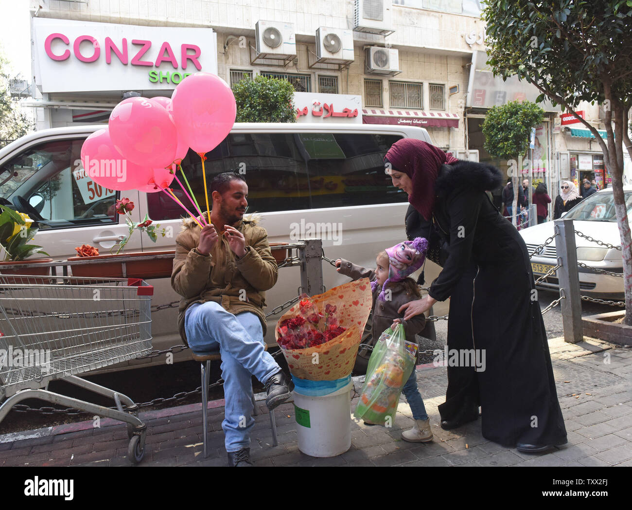A Palestinian girl approaches a vendor selling balloons and red flowers ...
