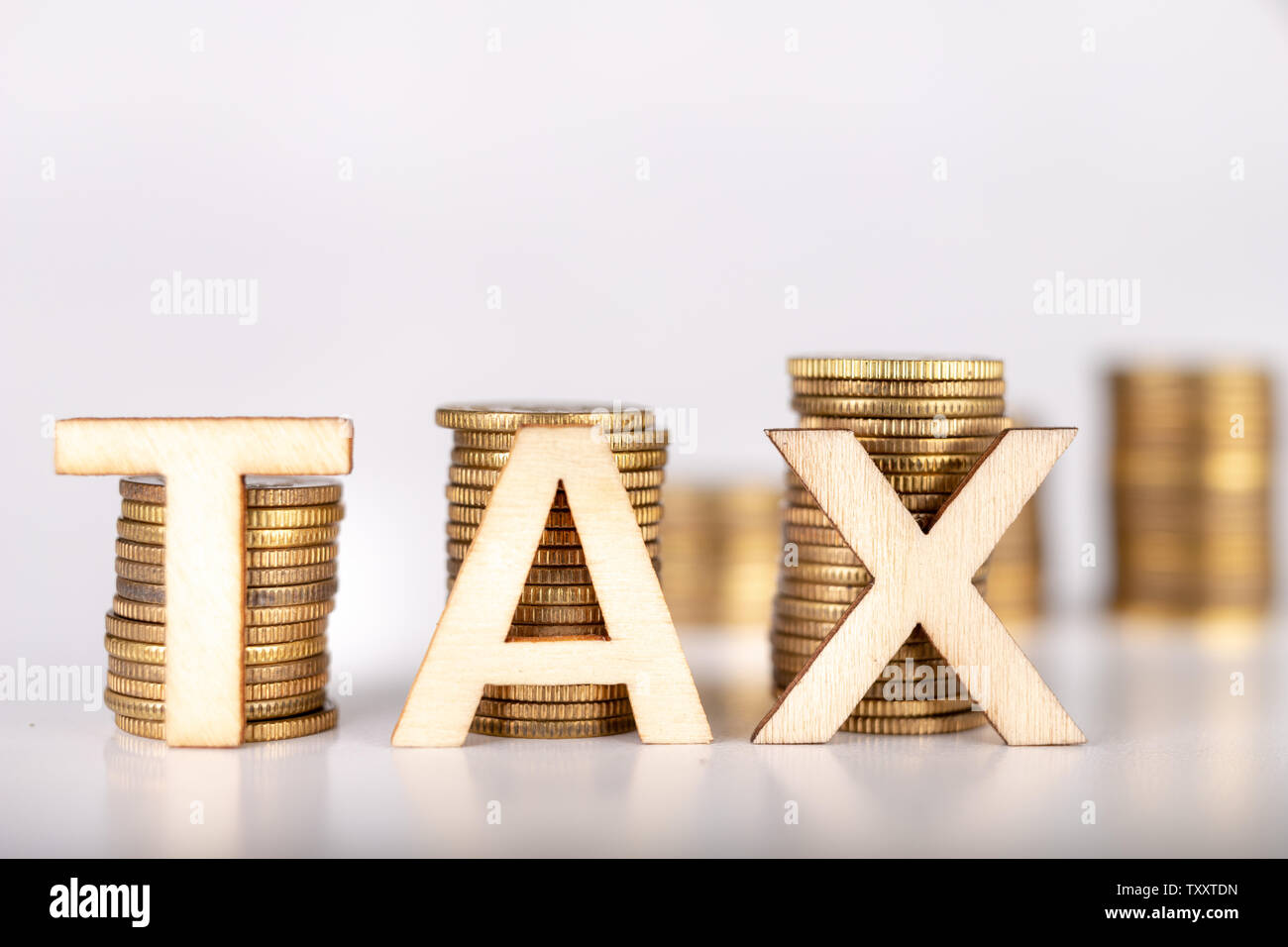 Bars stacked from coins on a white table. TAX lettering with wooden ...