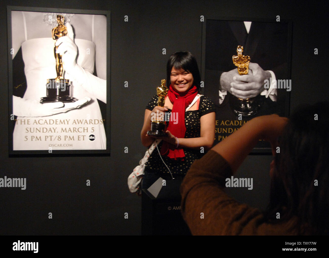 A visitor poses with an Oscar statuette tethered to a stand as part of ...