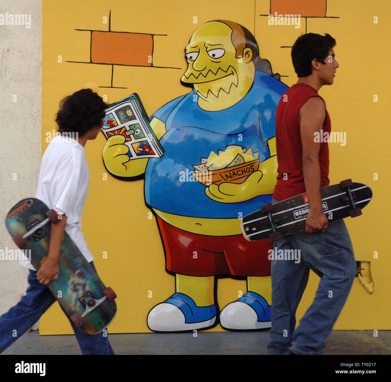 Skateboarders walk past a cutout of "Simpson" character Comic Book Guy ...