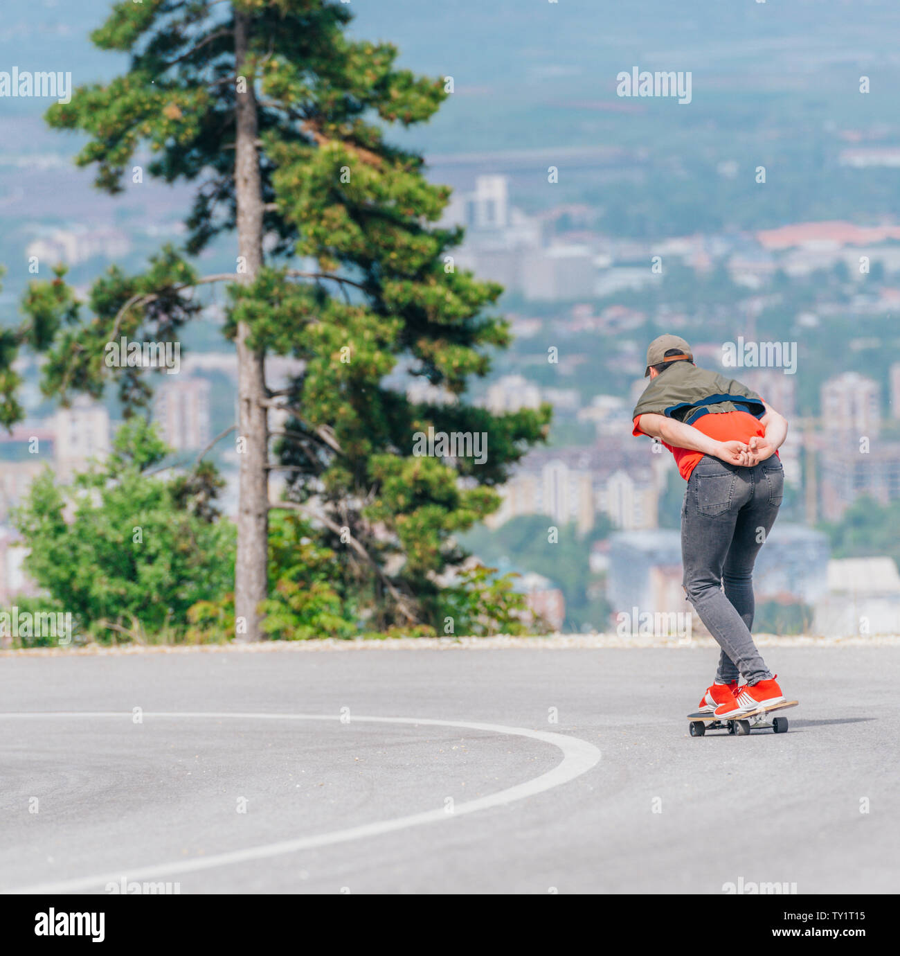 Tall athlete riding his longboard fast and steady downhill while ...
