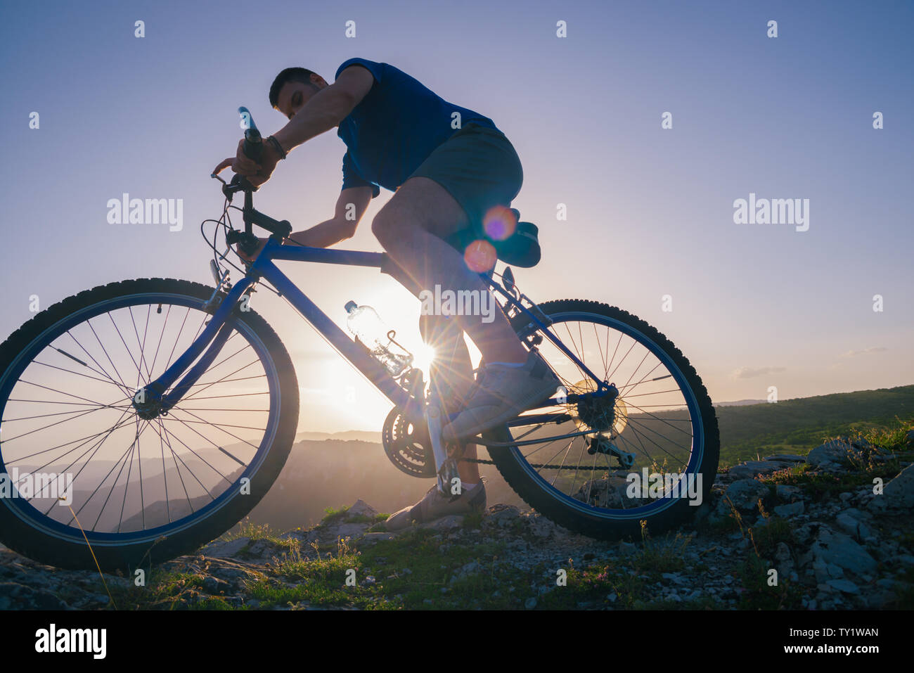 Strong fit male mountain biker performing stunts on rocky terrain on a ...