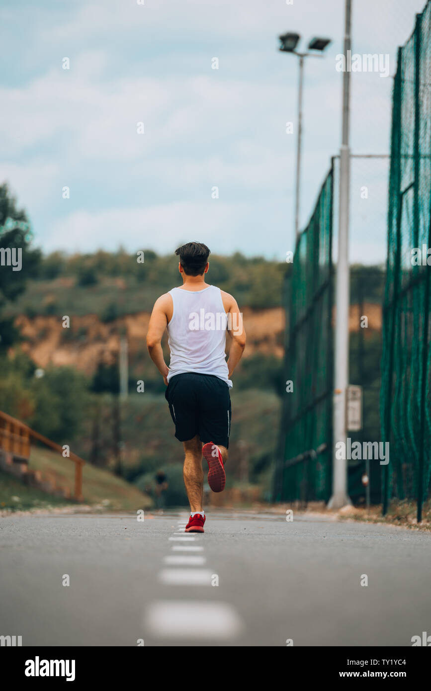 Handsome young man running and jogging on road in a sunny day, wearing ...