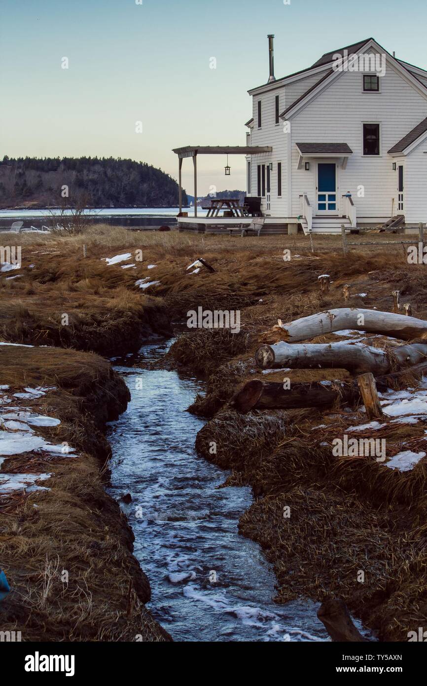 Little stream flowing through the land by a big white house with forest ...