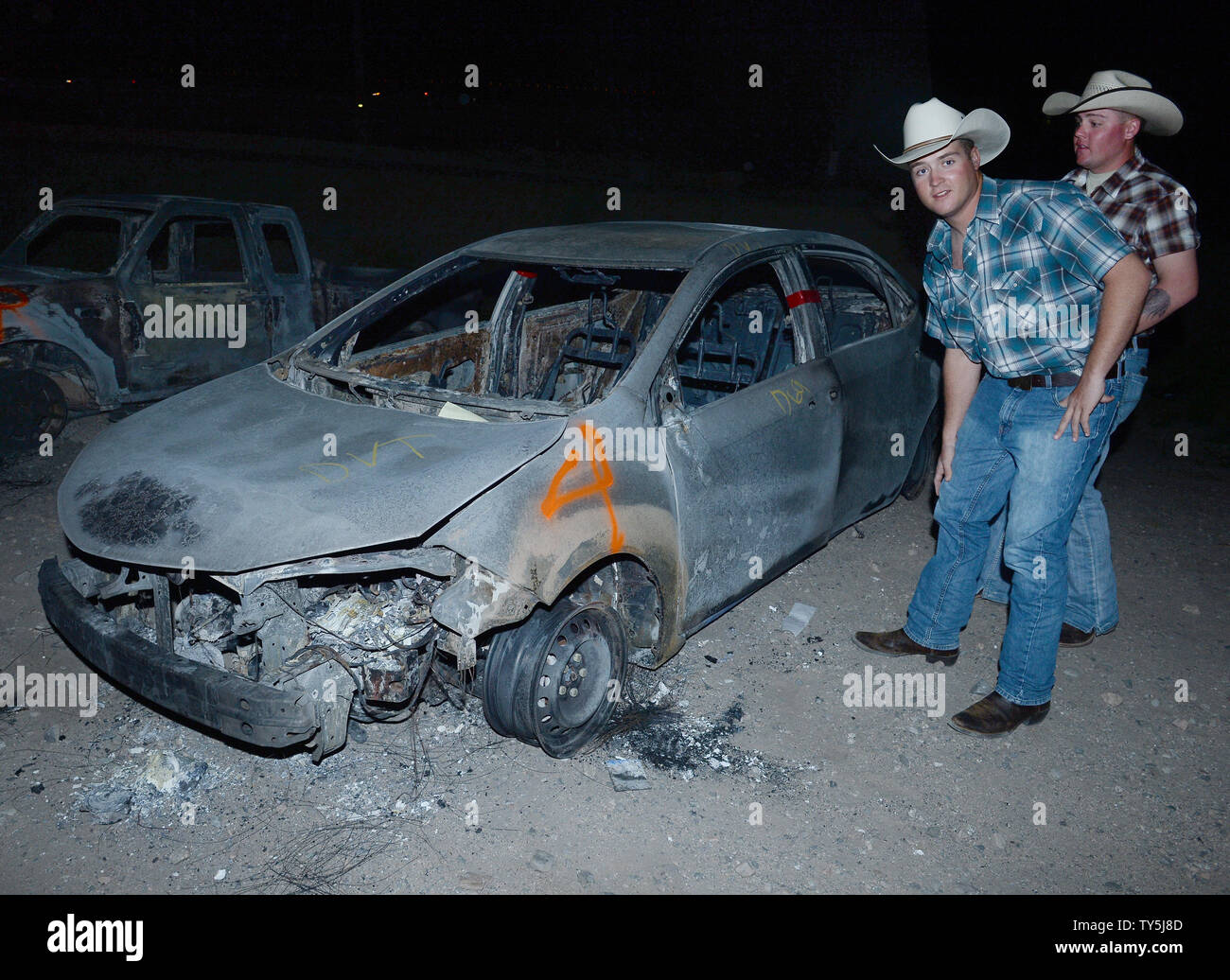 Two men examine one of 30 cars destroyed when a brush fire spread to ...