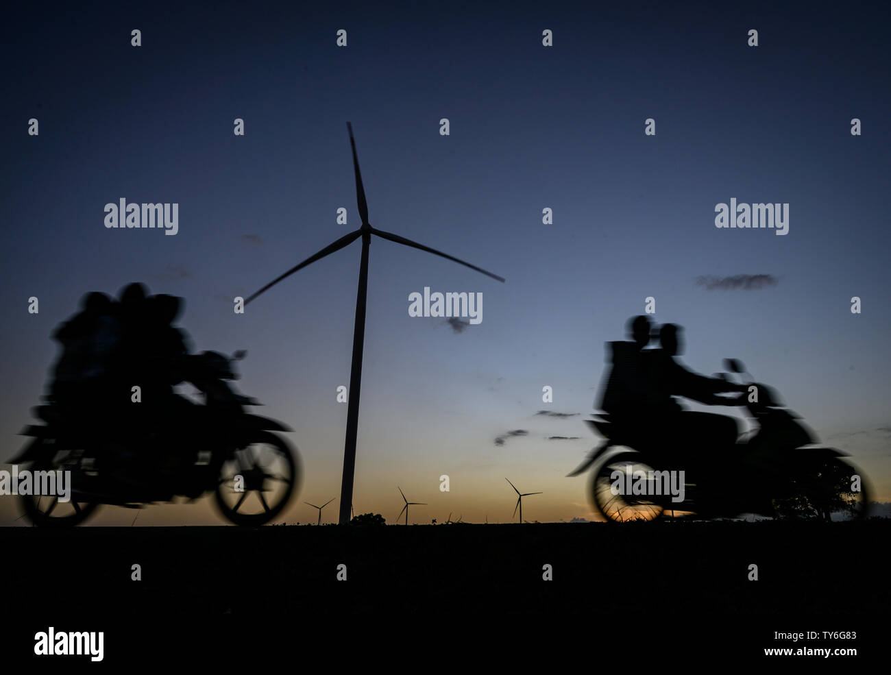 Jeneponto, Indonesia. 23rd June, 2019. Residents ride past the turbines ...