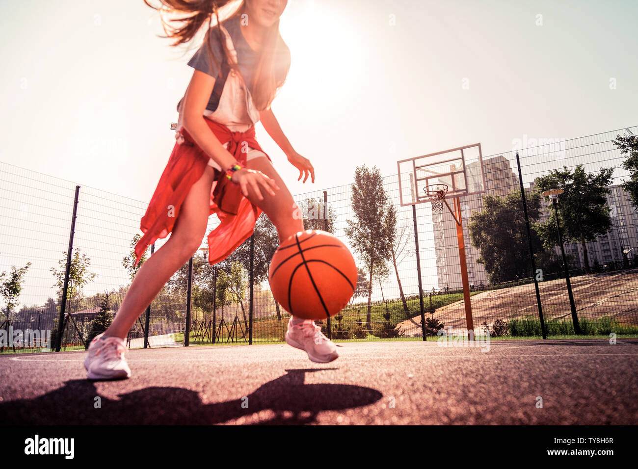 Experienced dark-haired young girl running around basketball playground ...