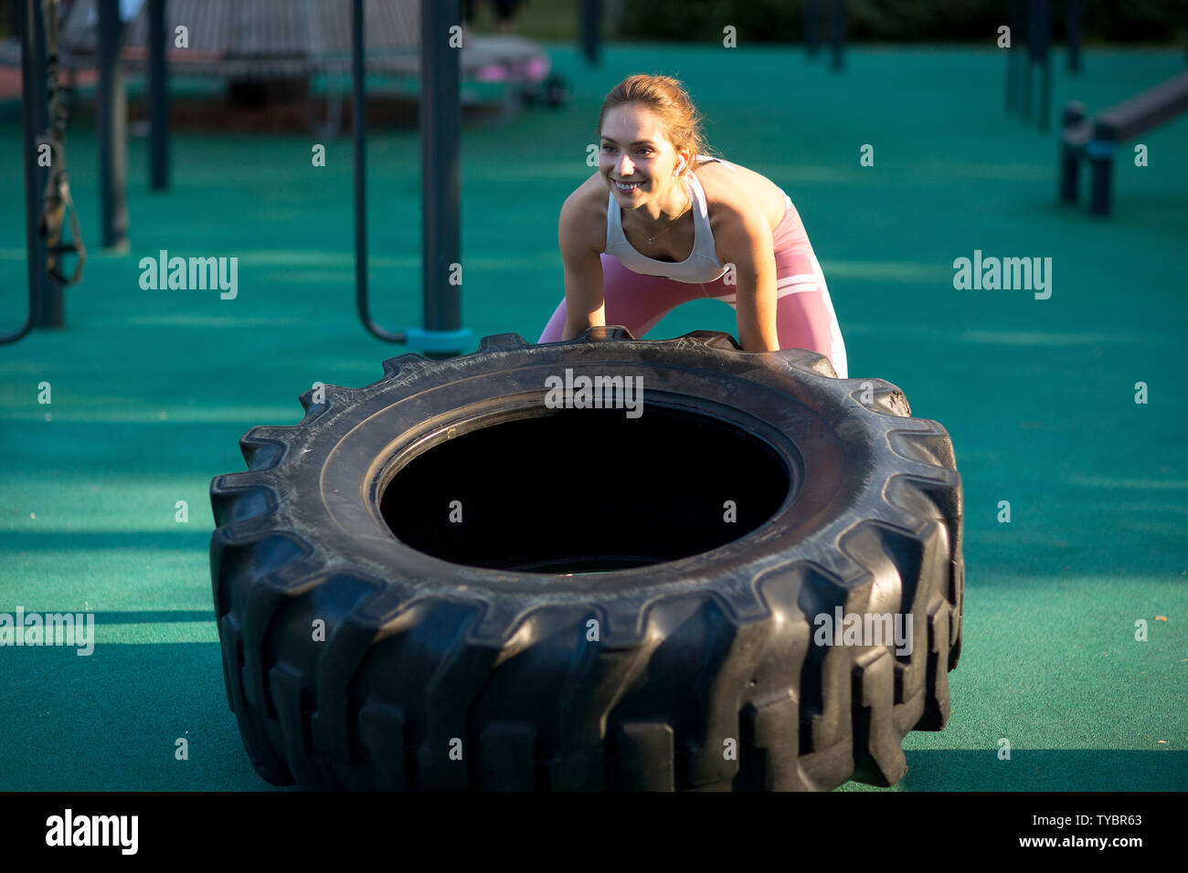 Young woman is training with tire on the outdoor playground. Gym open ...