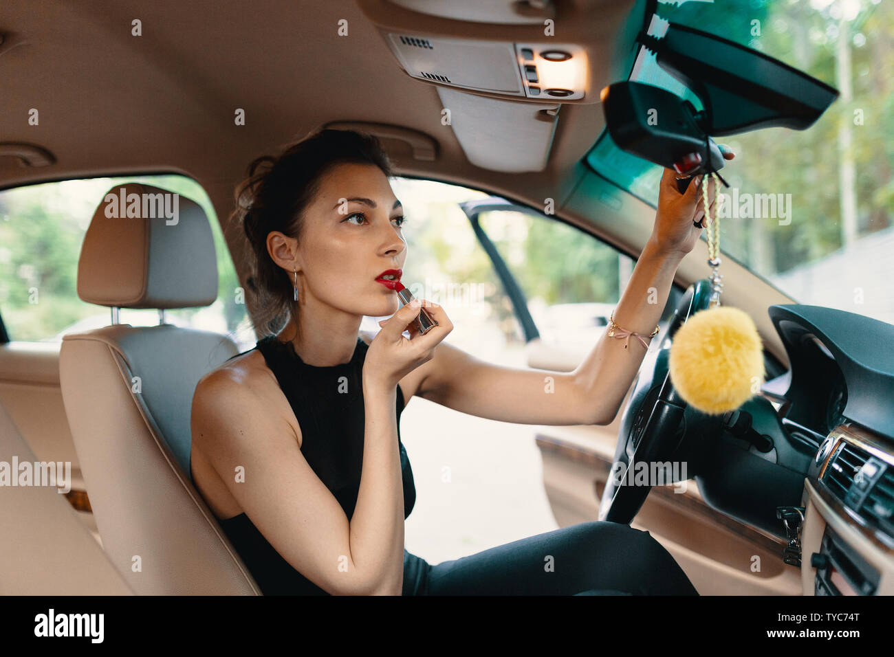 Young elegant woman looking in rear view mirror painting her lips doing ...