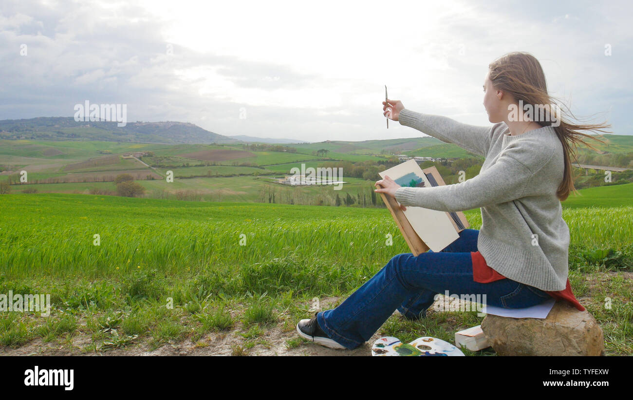 A talented woman sits on the field and drawing - measures the ...
