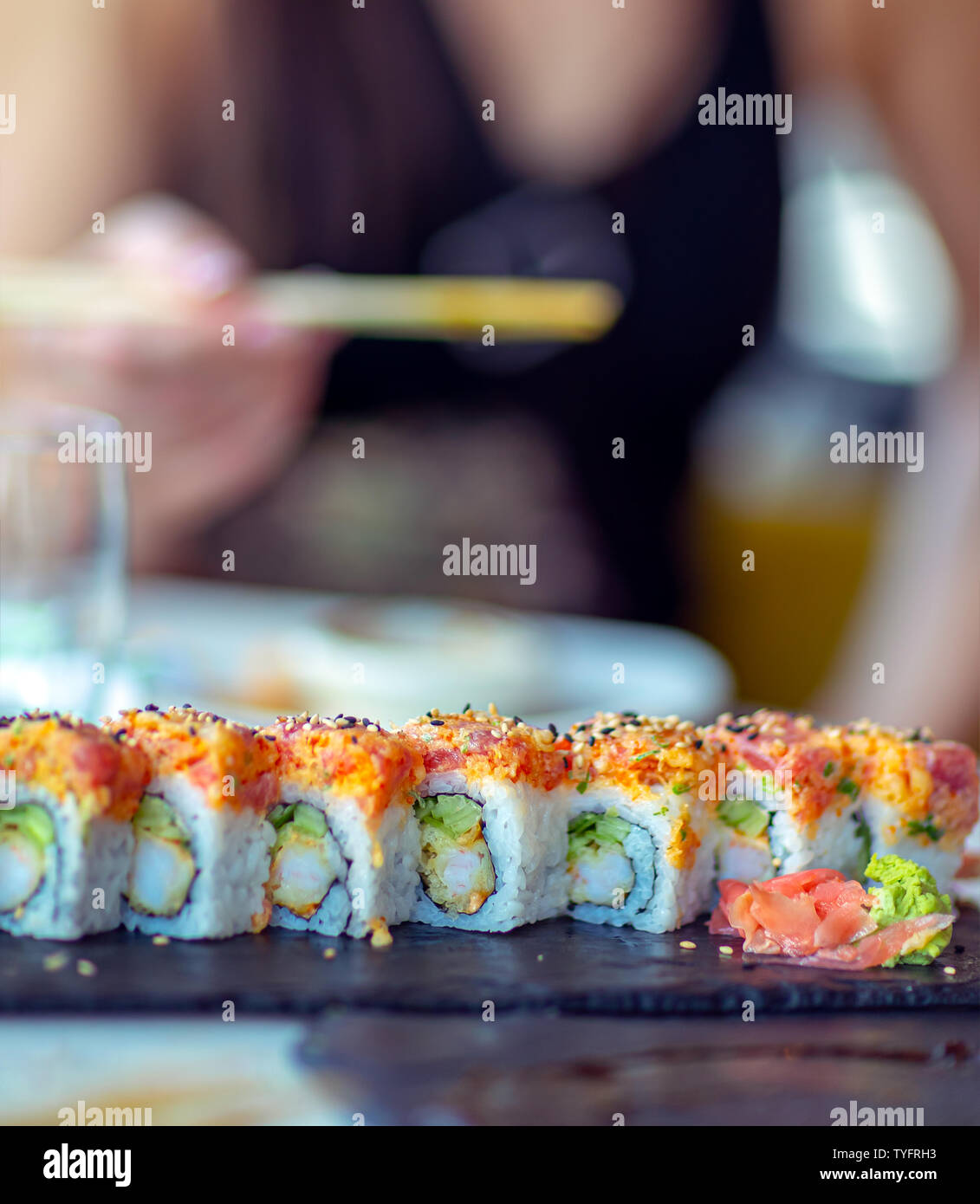 Eating sushi in the restaurant, a woman using chopsticks takes a piece ...