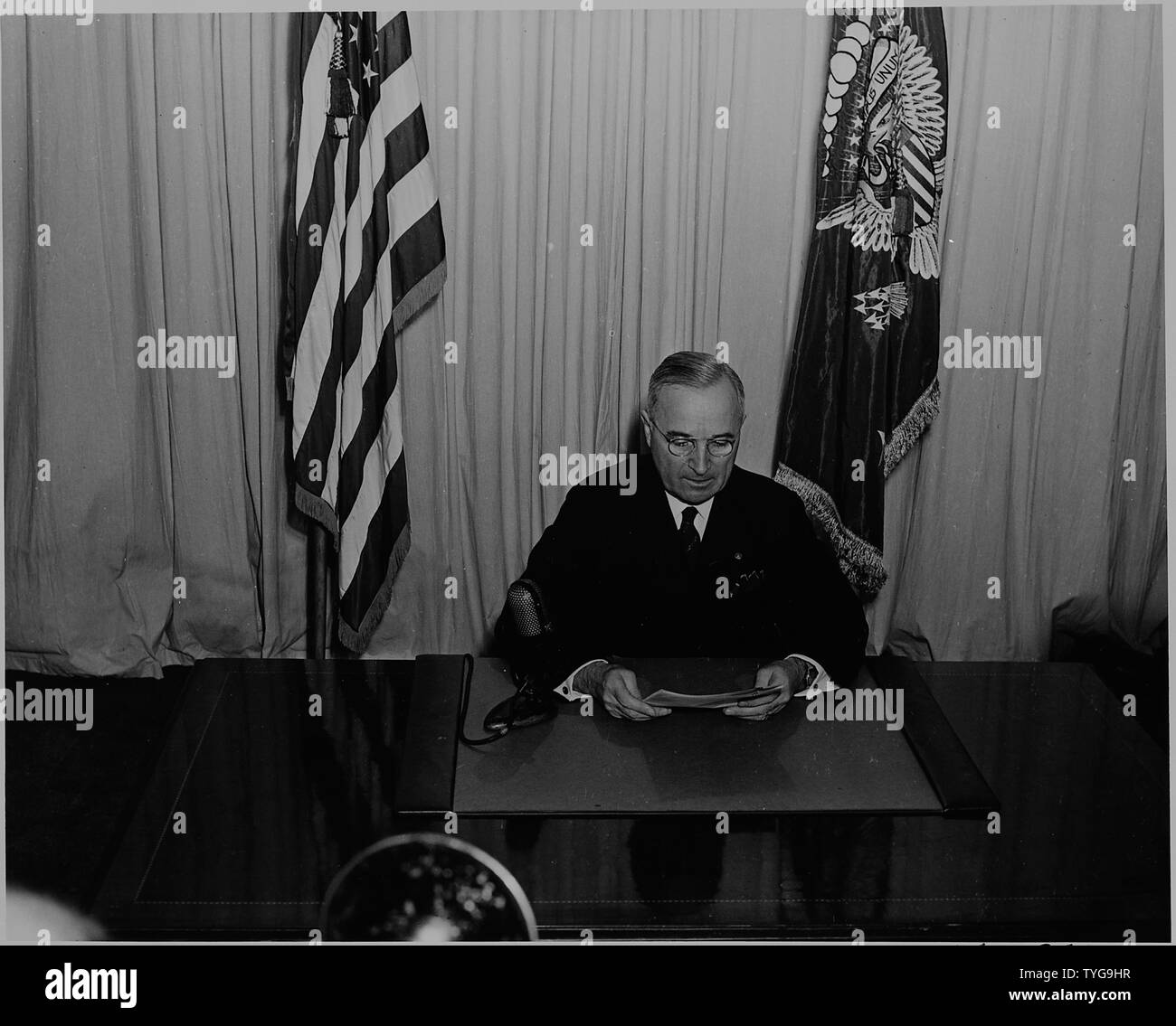 President Harry S. Truman seated at a desk, before a microphone ...