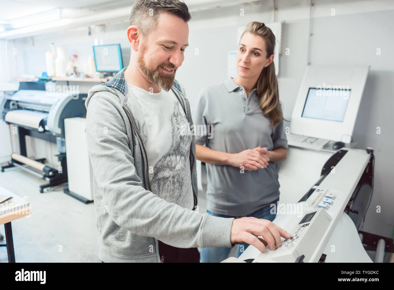 Two employees in advertising agency operating large format printer ...