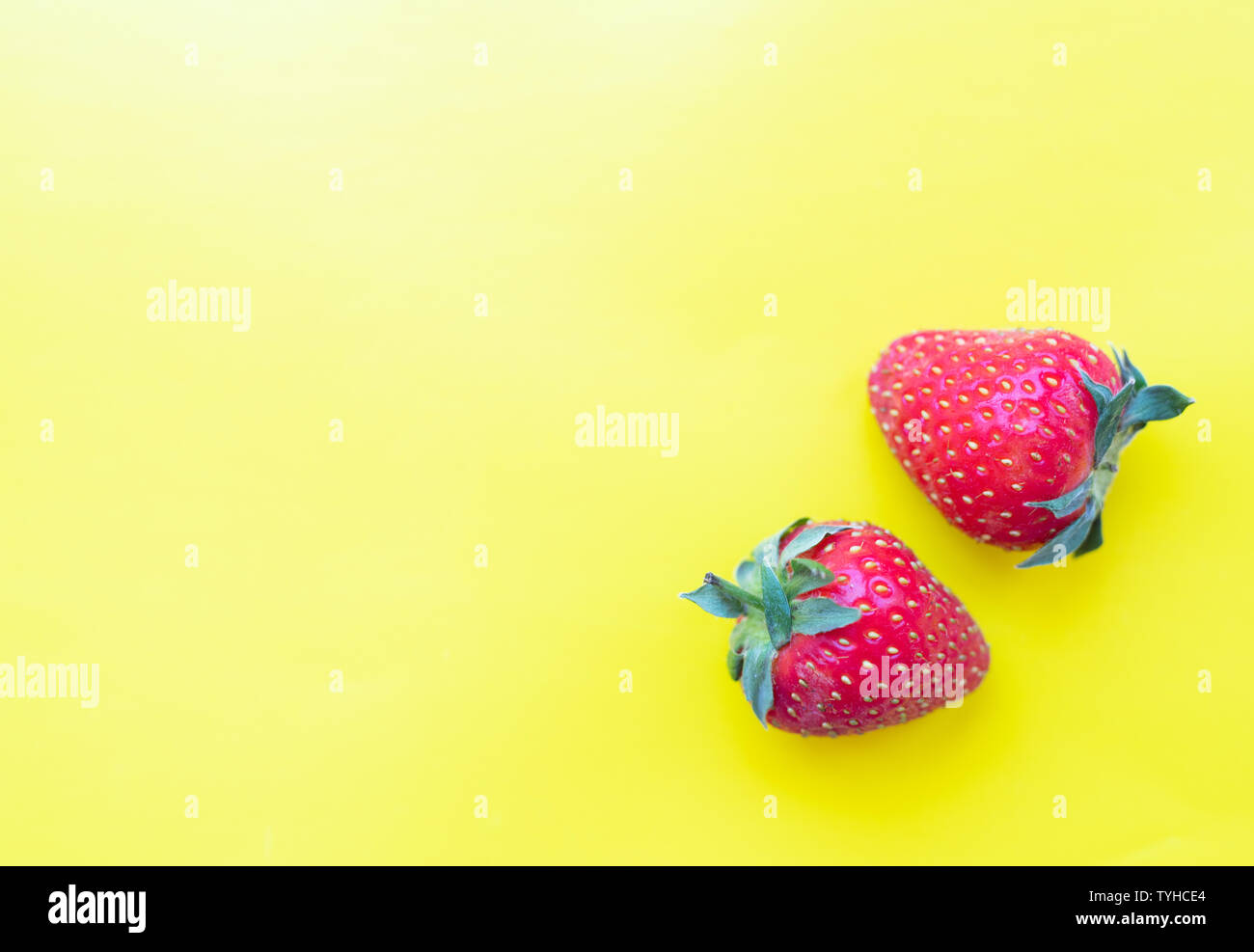 two strawberries on a bright yellow background Stock Photo - Alamy