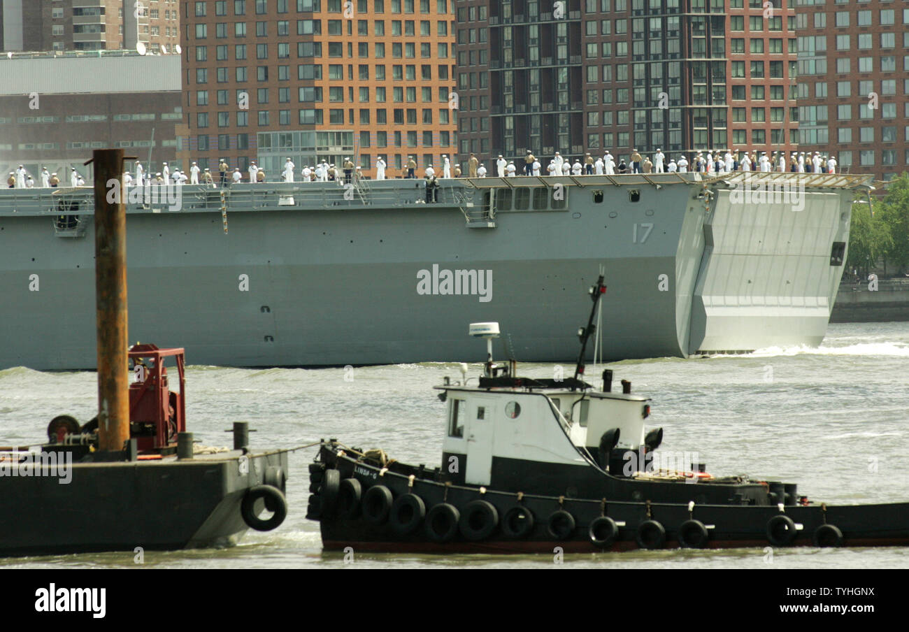 Sailors standing on the deck of a US Navy ship pass by a moored barge ...
