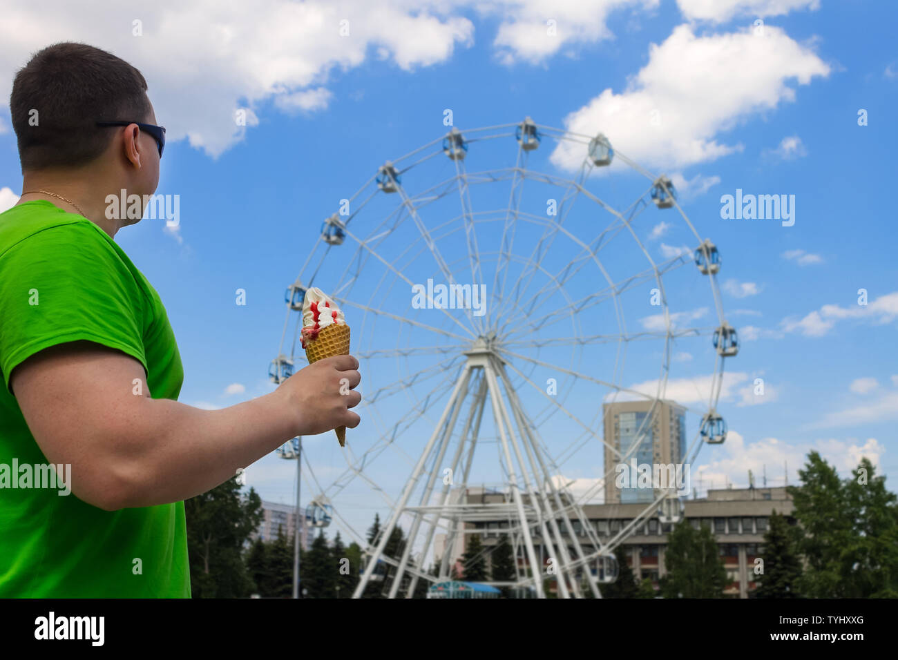 A man with an ice cream in his hand is standing in an amusement park ...