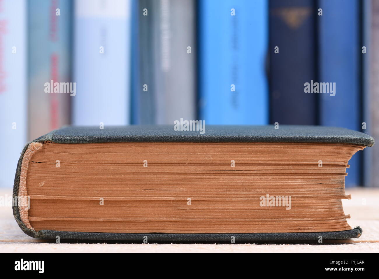 Closed book on wooden deck with blurred bookshelf in the background ...