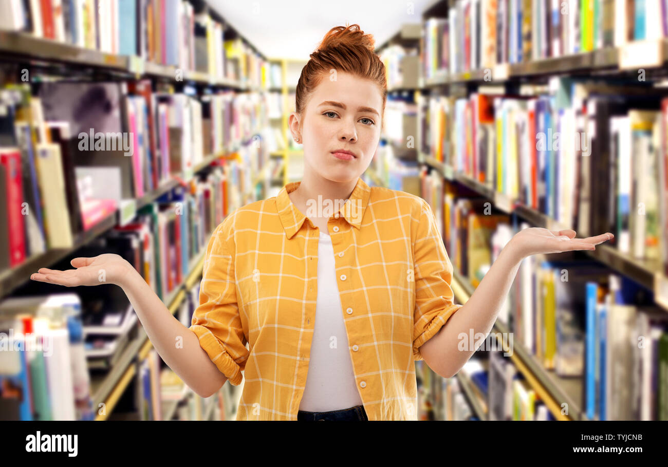 sad red haired student girl shrugging at library Stock Photo - Alamy